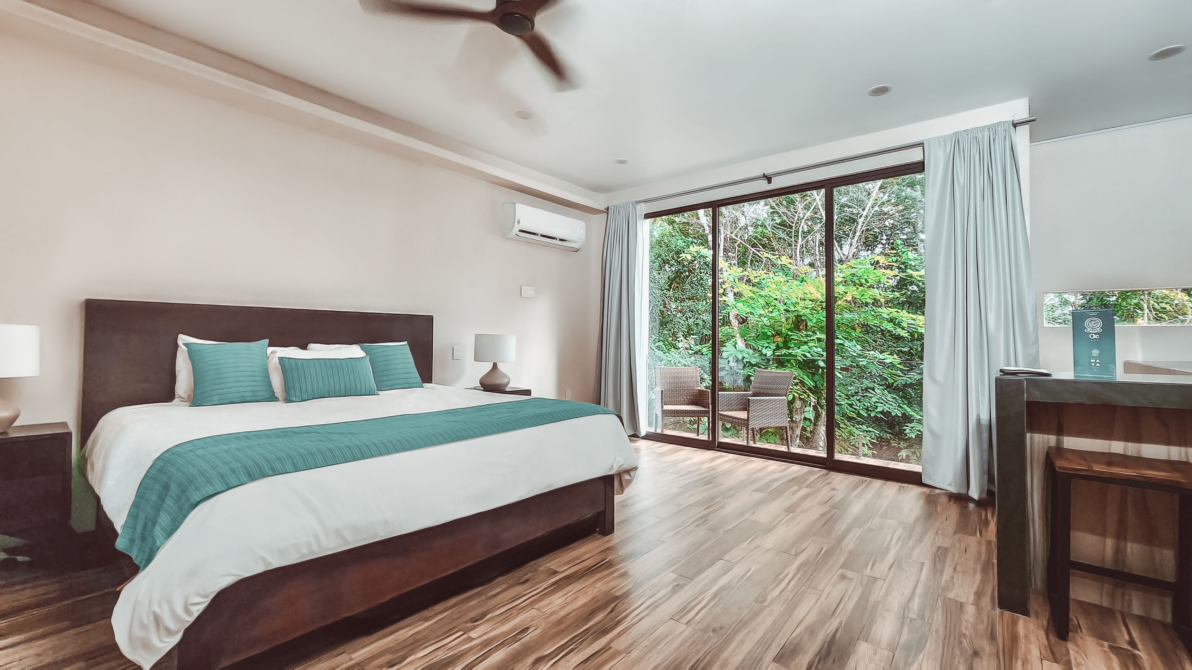 Quarto de hotel moderno com uma cama grande, um ventilador de teto, uma escrivaninha e vista para o exterior.