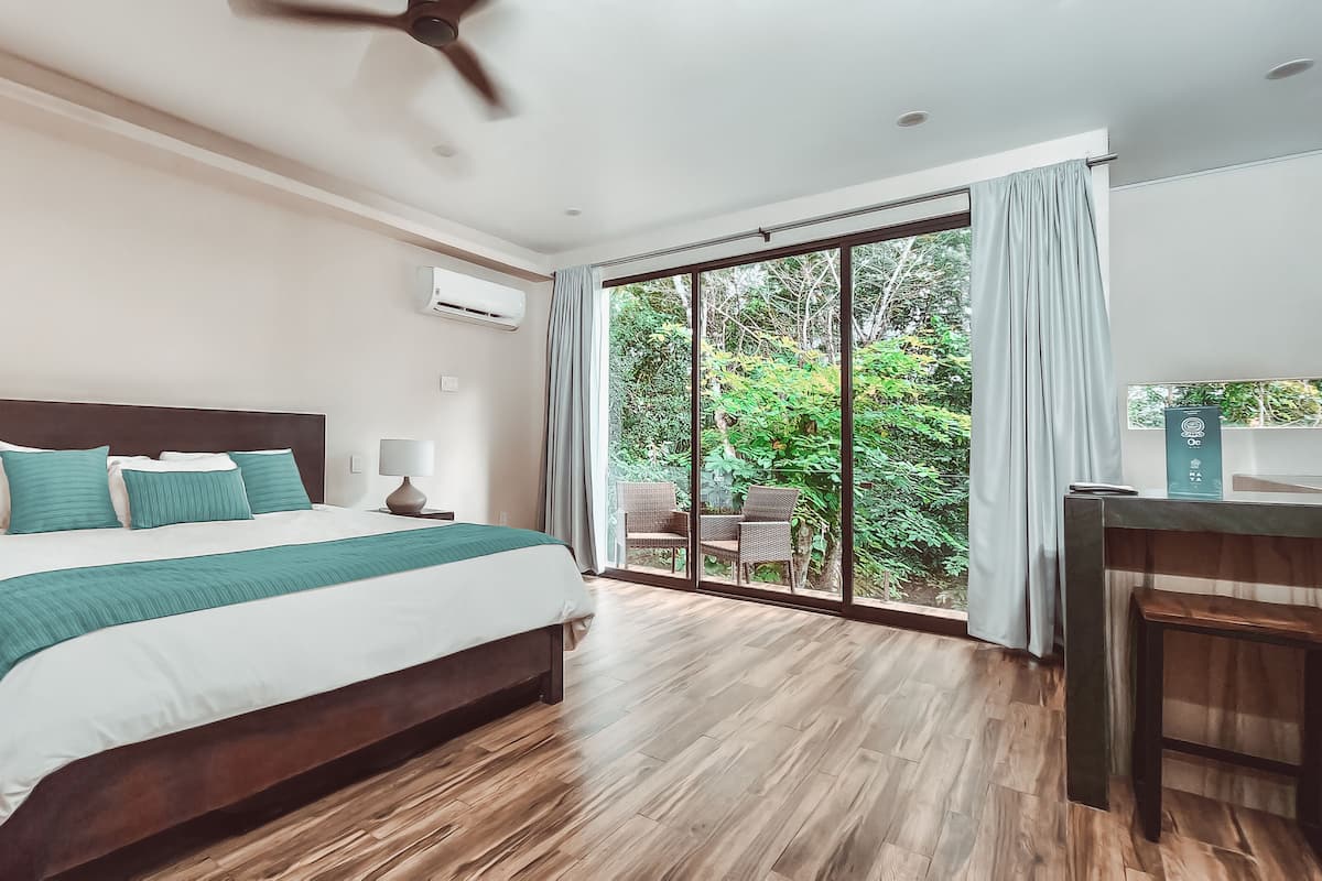 Quarto de hotel moderno com uma cama grande, um ventilador de teto, uma escrivaninha e vista para o exterior.