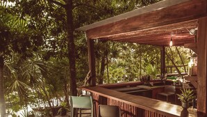 Um deck de madeira com área de bar, duas cadeiras e vista para vegetação exuberante.