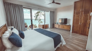 Quarto com cama grande, televisão, guarda-roupa de madeira e varanda com vista.