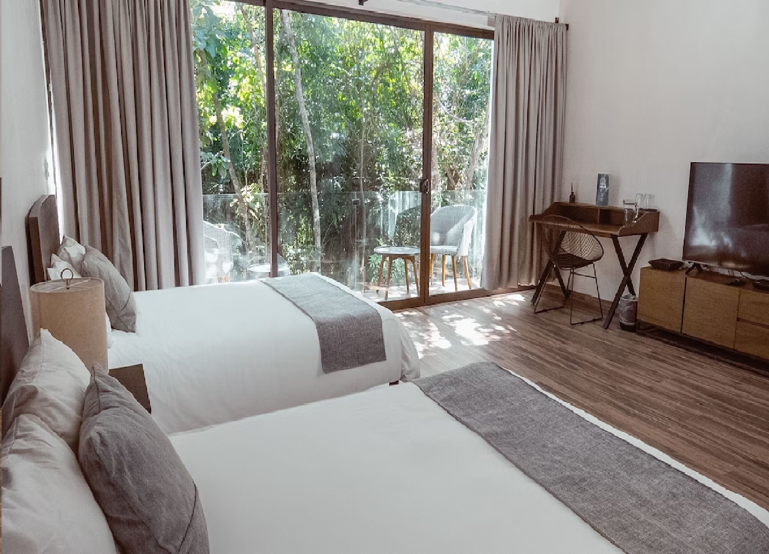 Quarto com cama grande, escrivaninha, televisão e vista para área verde através de uma porta de vidro deslizante.