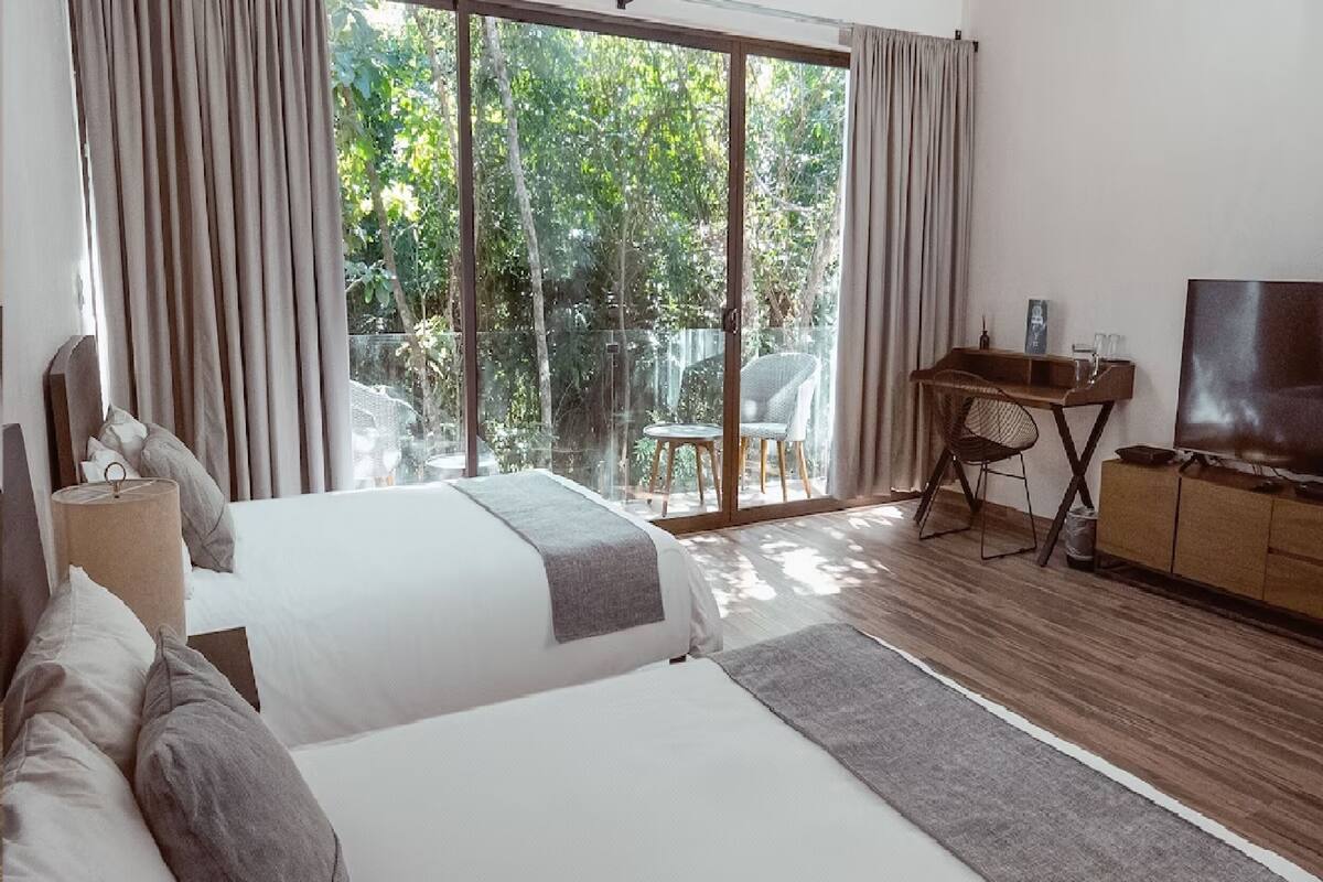 Quarto com cama grande, escrivaninha, televisão e vista para área verde através de uma porta de vidro deslizante.
