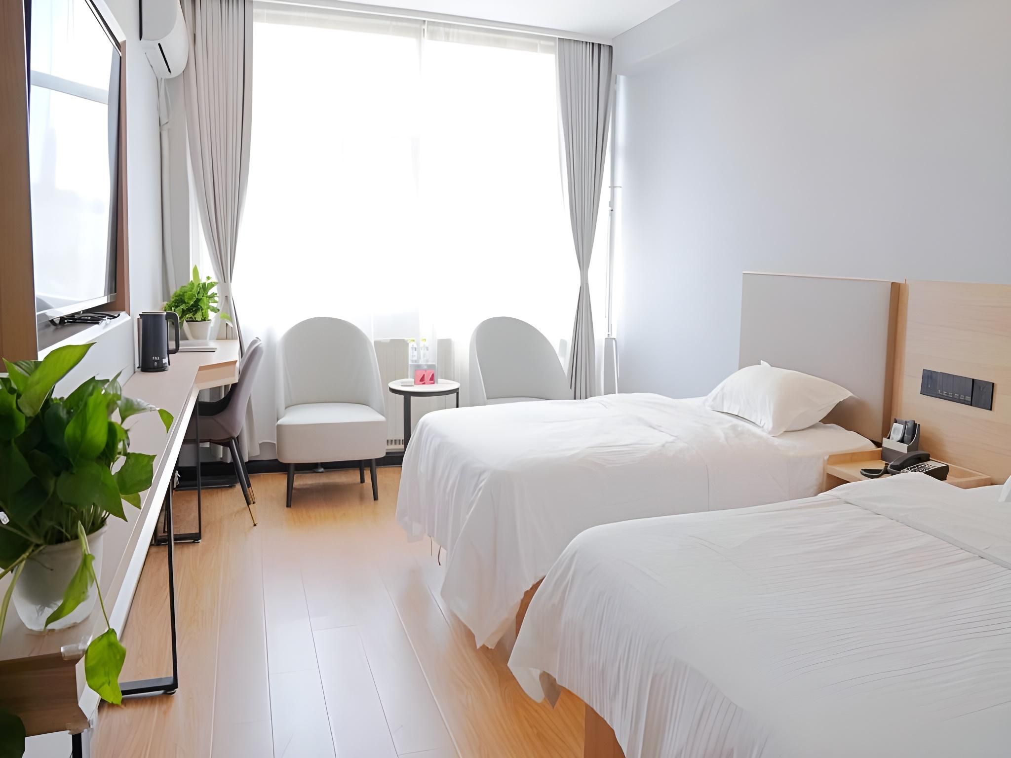 Quarto de hotel com duas camas, uma escrivaninha, cadeiras, uma mesinha e um vaso de planta.