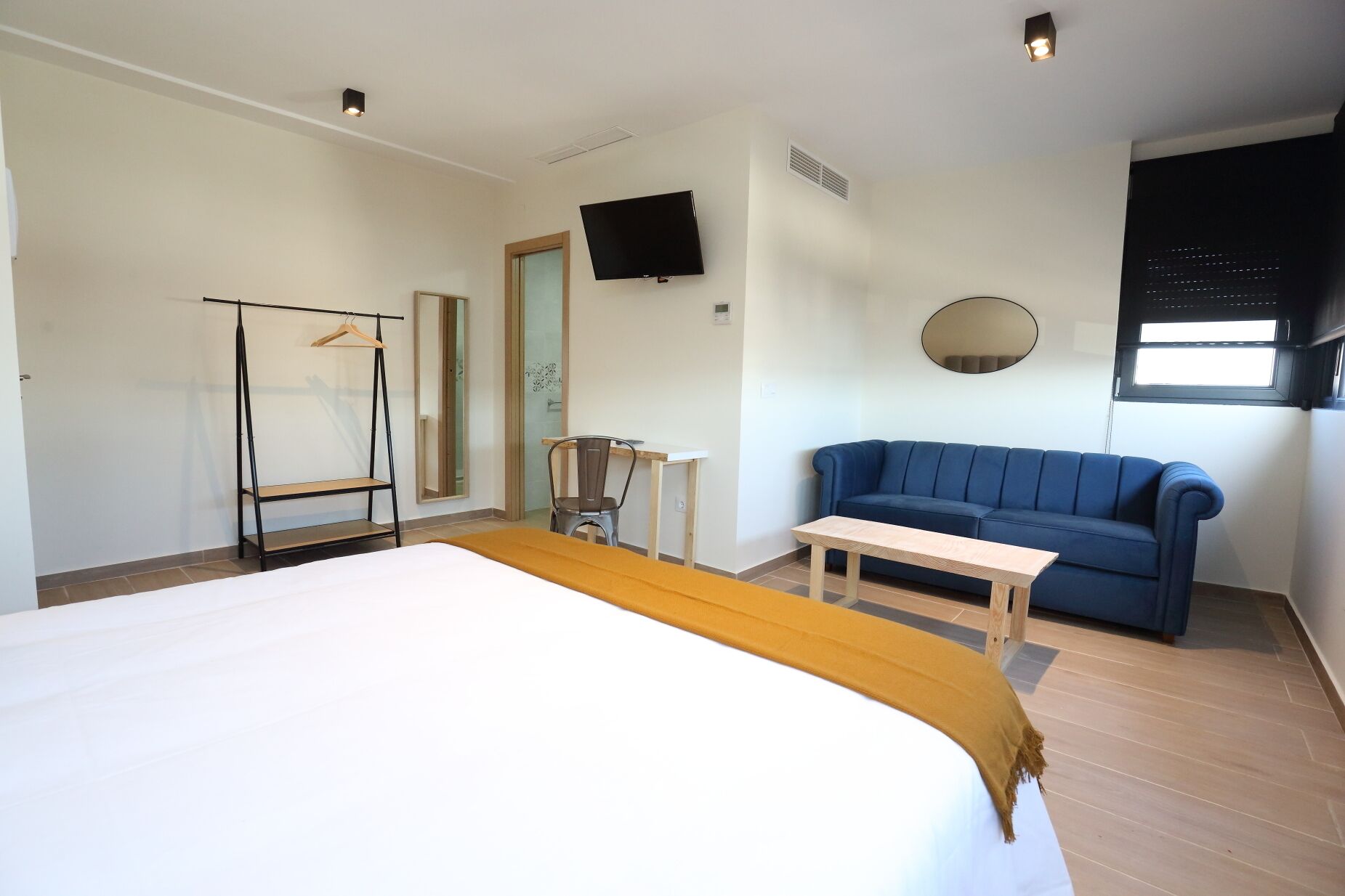 Quarto de hotel com uma cama, um sofá azul, uma mesa pequena, uma televisão e um guarda-roupa.