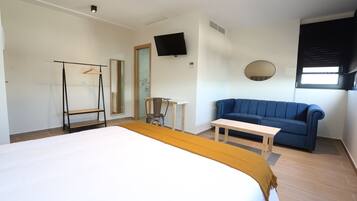 Quarto de hotel com uma cama, um sofá azul, uma mesa pequena, uma televisão e um guarda-roupa.