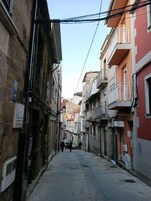 Uma rua estreita com edifícios em ambos os lados, com varandas e uma mistura de estilos arquitetônicos.
