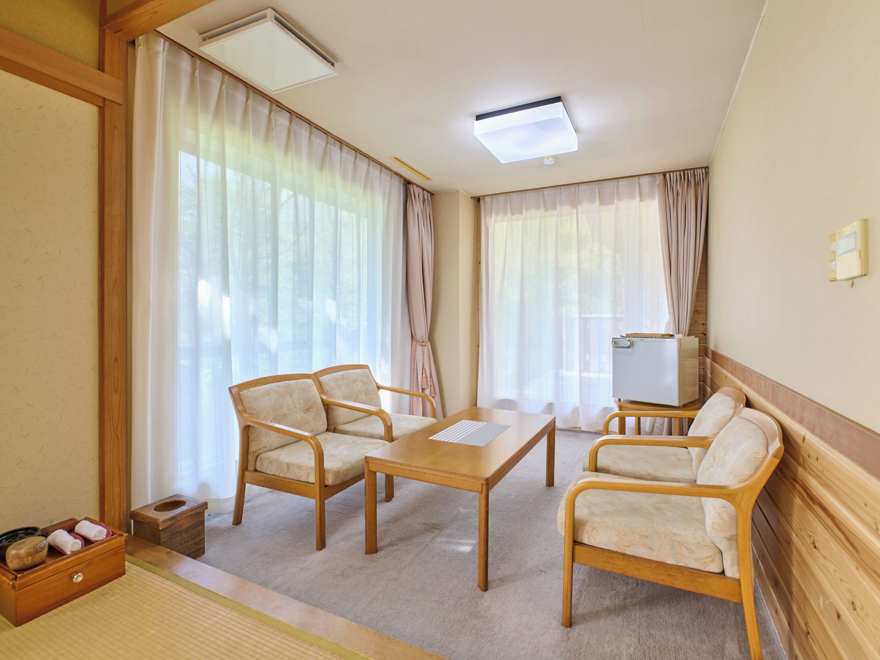 Quarto com piso de madeira, uma mesa de madeira, duas cadeiras de madeira, um pequeno armário de madeira e um radiador branco.