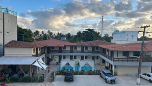 Um edifício de dois andares com telhado de telhas vermelhas, piscina e um carro na entrada.