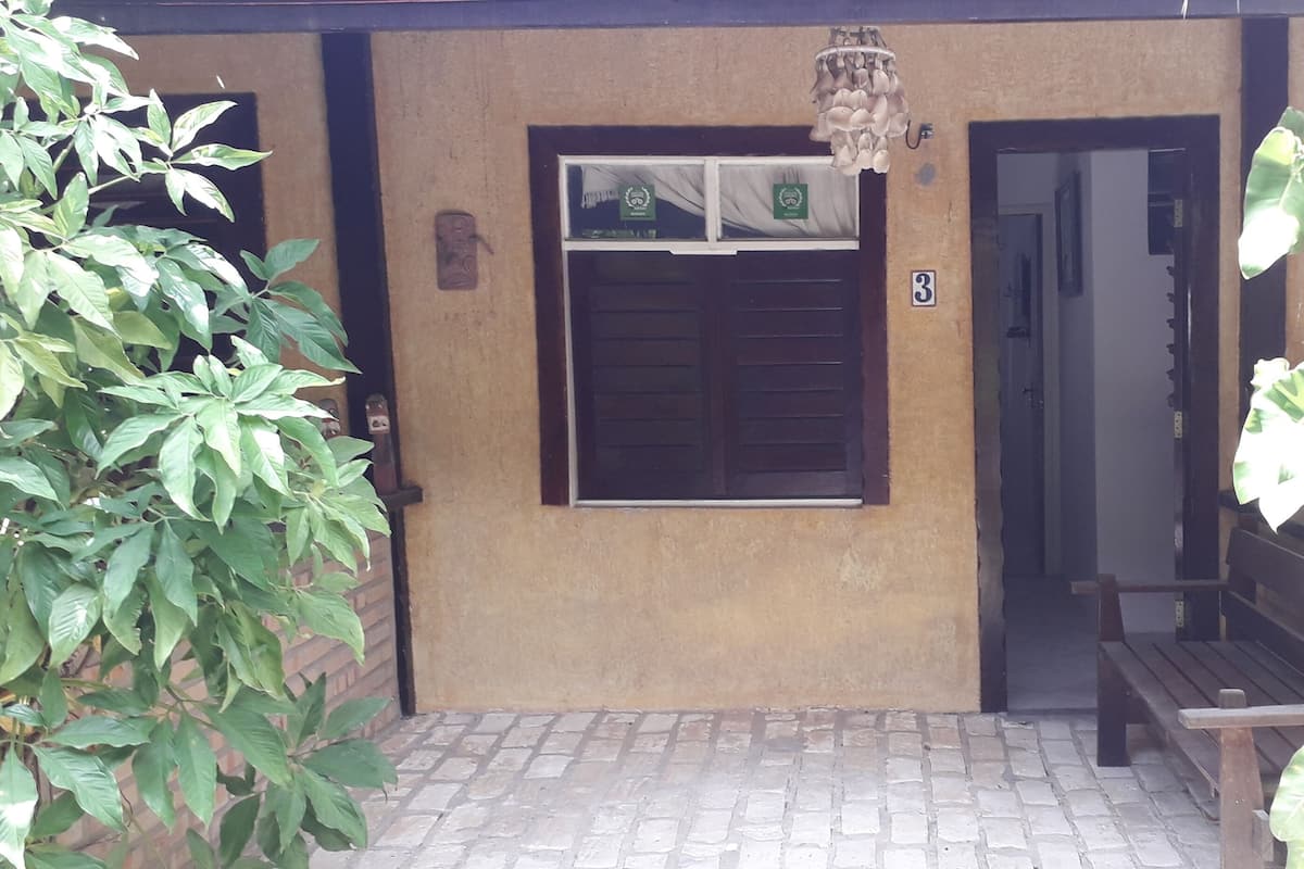 Entrada de um prédio com porta de madeira, placa com o número 3 e um banco na parte externa.