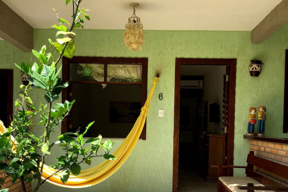Uma área externa coberta com uma rede, um banco e uma porta que dá para o interior.