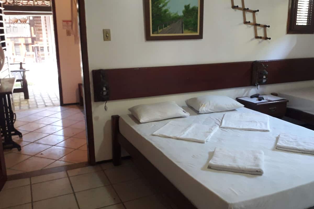 Quarto de hotel com uma cama grande, mesa de cabeceira, prateleira e nicho na parede.
