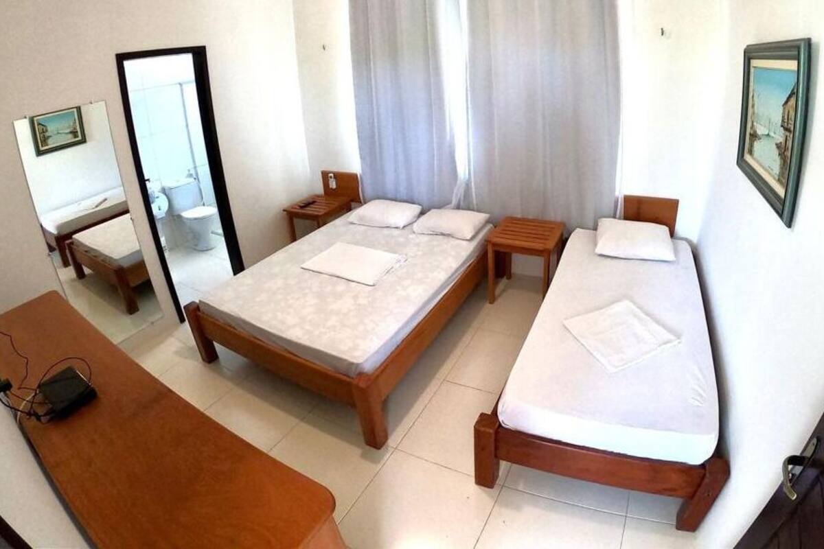 Quarto de hotel com duas camas de solteiro, uma escrivaninha de madeira, um espelho e uma mesinha.