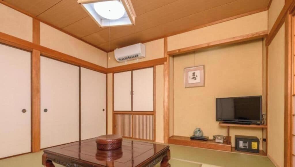 Um quarto japonês tradicional com tatames, uma mesa de madeira, uma televisão e uma porta deslizante.