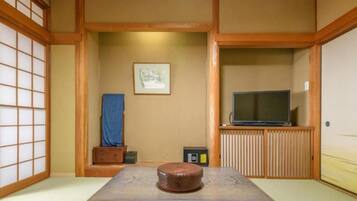 Um quarto japonês tradicional com tatames, uma mesa baixa com uma cesta de palha, uma televisão sobre um suporte de madeira e uma porta deslizante.
