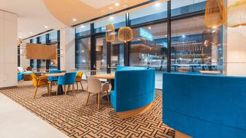 Restaurante moderno com assentos azuis, mesas de madeira e piso estampado.
