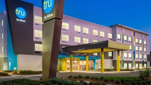 Um hotel moderno com uma placa de 'tru by Hilton' bem visível, uma entrada coberta e céu claro.