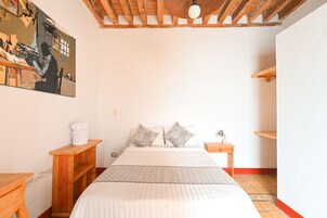 Quarto com cama, mesas de cabeceira de madeira, um quadro na parede e ventilador de teto.