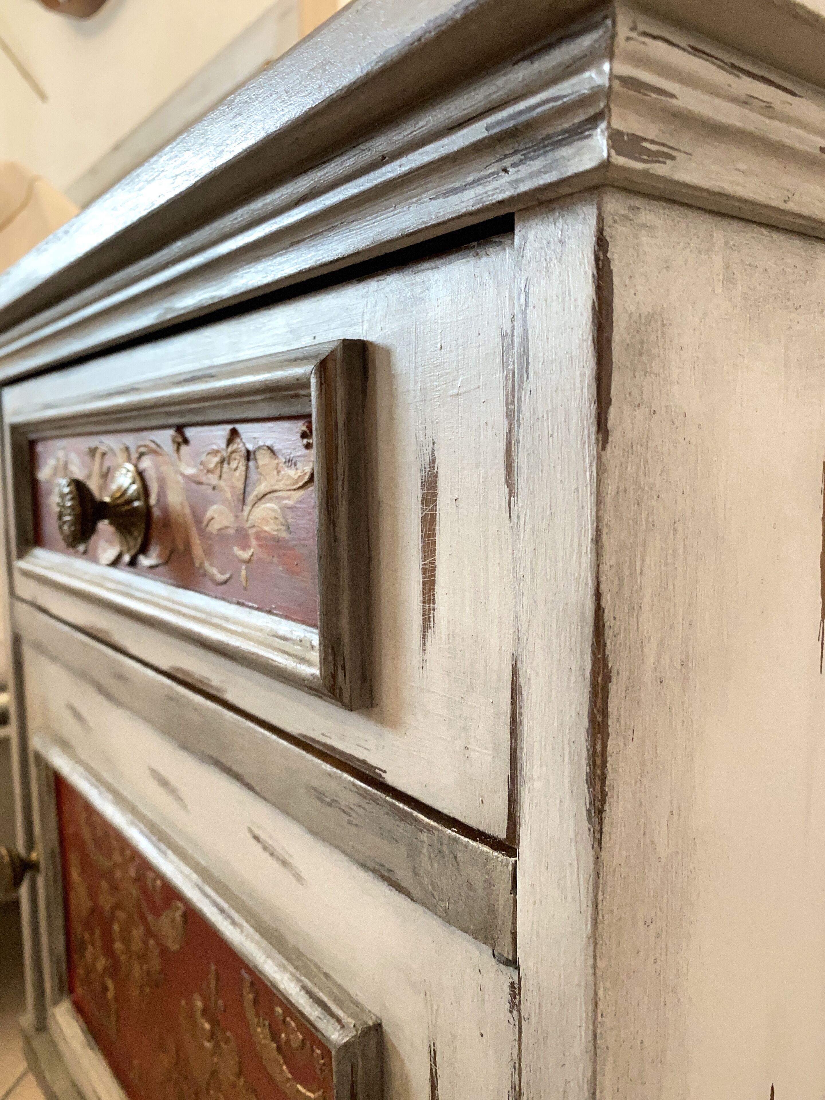 Um close-up de uma cômoda com um painel decorativo e uma gaveta com puxador de latão.