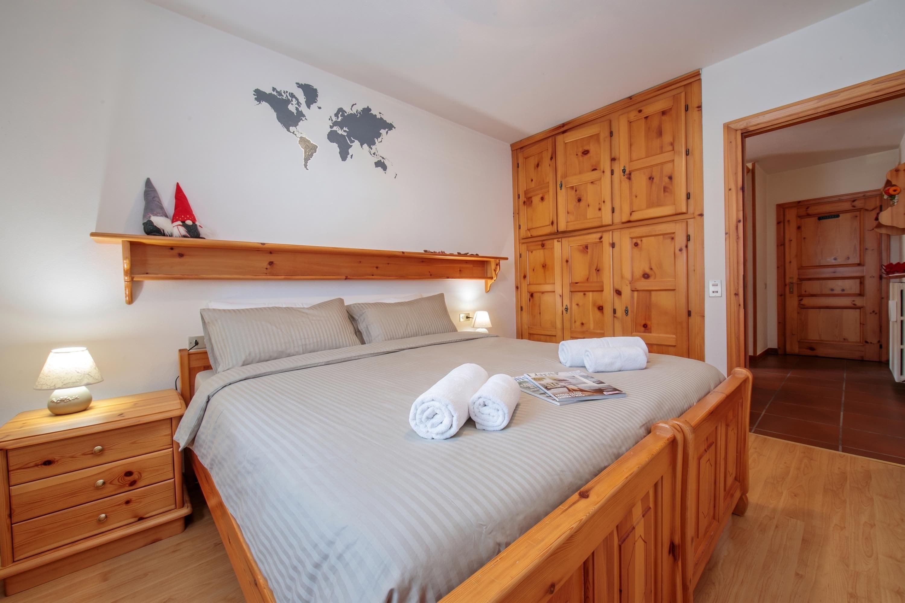 Quarto bem arrumado com cama, mesas de cabeceira, guarda-roupa de madeira e um mapa-múndi na parede.