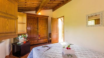 Um quarto com um guarda-roupa de madeira, uma mesa de cabeceira com um vaso de flores, uma cama com colcha florida e um espelho na parede.