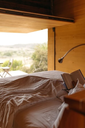 Uma cama, um livro, uma cadeira e vista para o exterior.