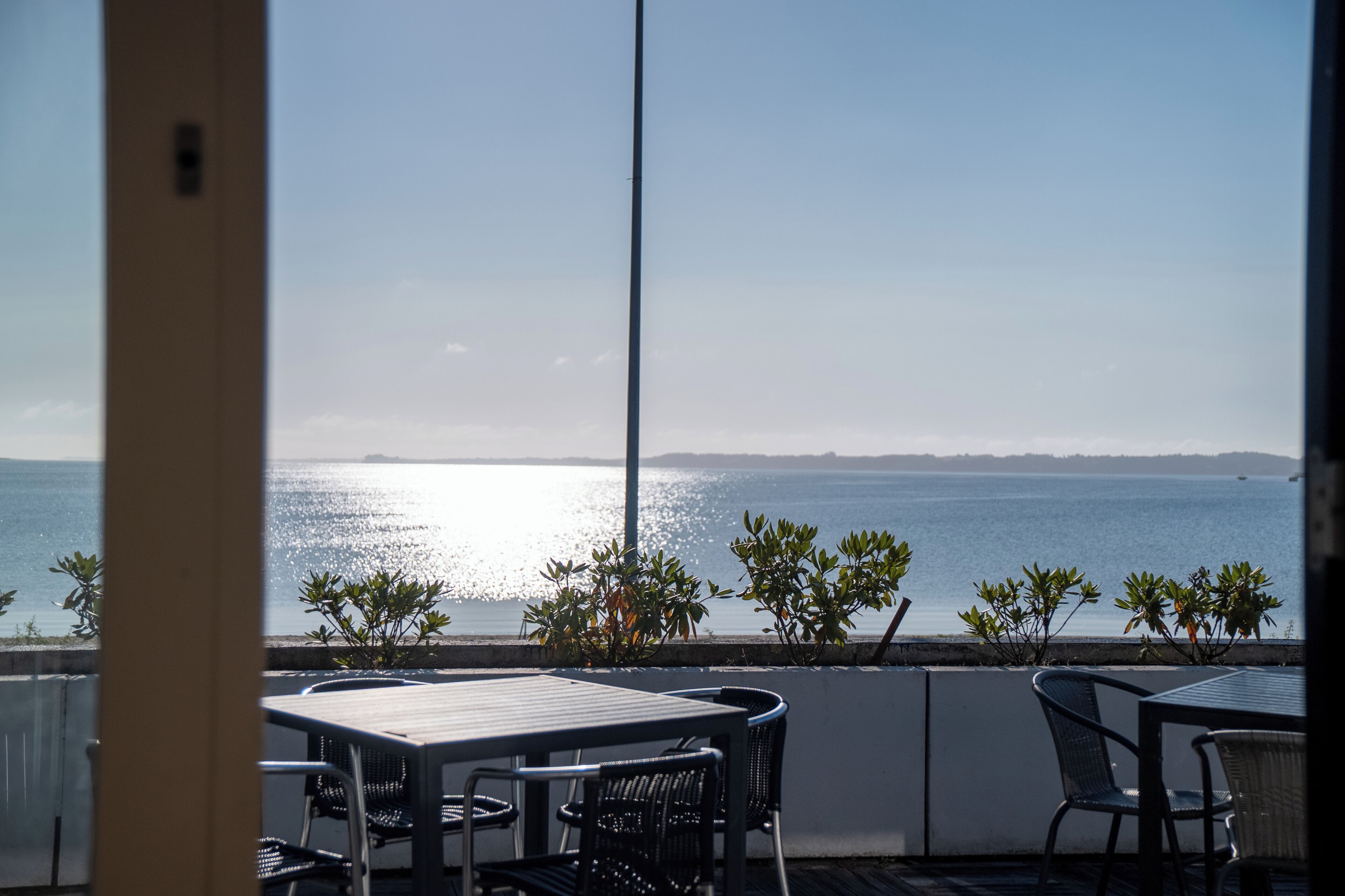 Terraço com mesa e cadeiras, com vista para um mar tranquilo e horizonte claro.