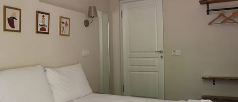 Quarto de hotel com uma cama, uma porta e um cabideiro.