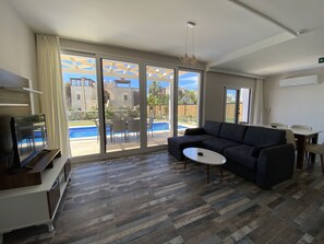 Uma sala de estar moderna vista para piscina, sofá, televisão e área de jantar.