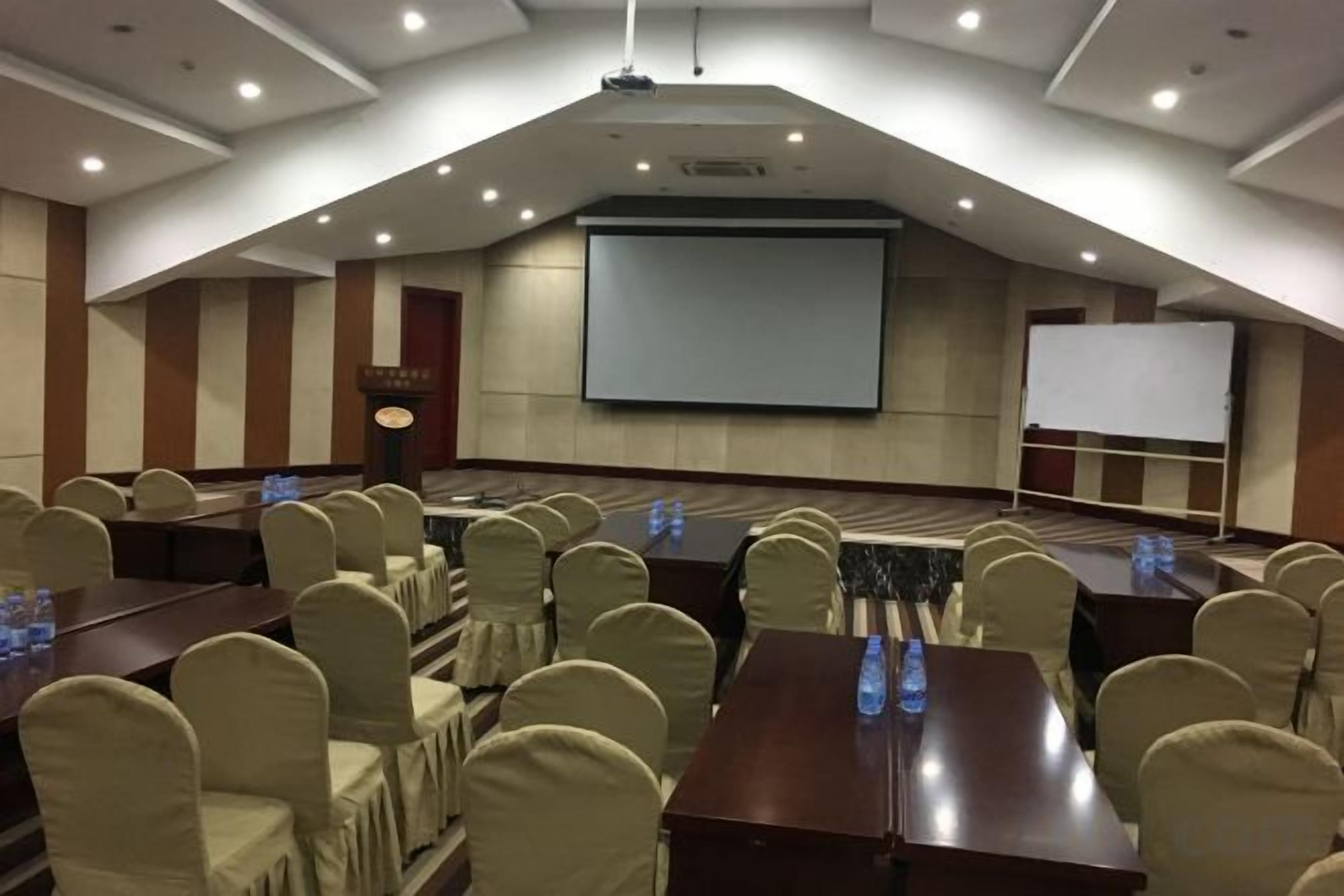 Uma sala de conferências com uma tela grande, várias mesas e cadeiras.
