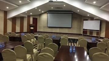 Uma sala de conferências com uma tela grande, várias mesas e cadeiras.