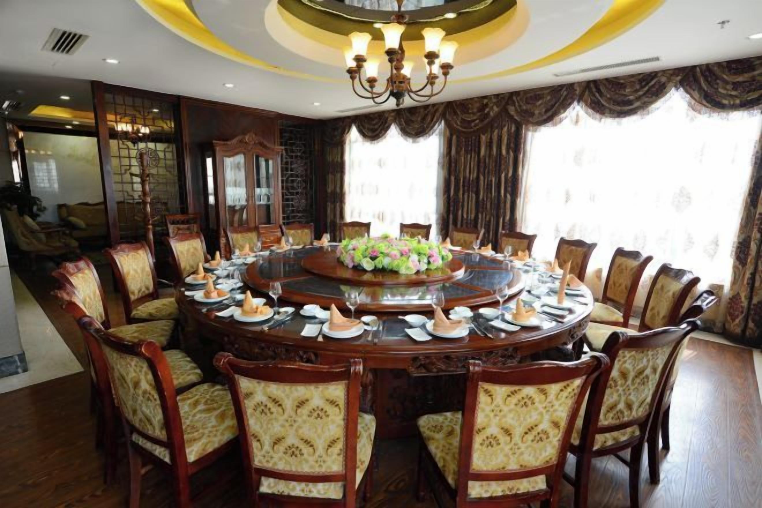 Mesa de jantar redonda com cadeiras, um lustre e um centro de mesa decorativo.