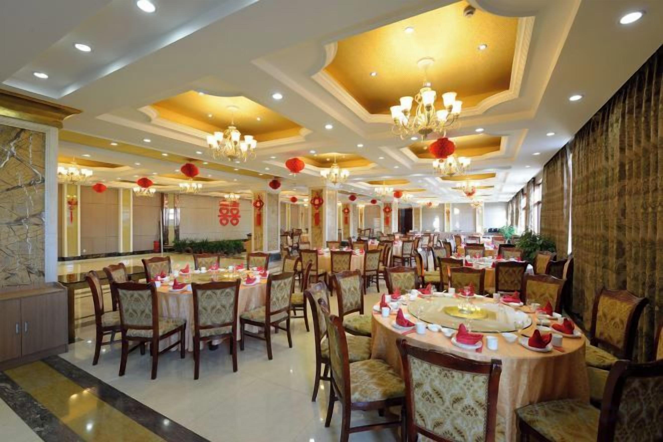 Uma sala de banquetes com mesas redondas, cadeiras, lustres e lanternas vermelhas.