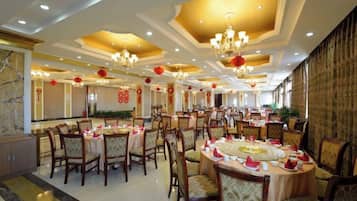 Uma sala de banquetes com mesas redondas, cadeiras, lustres e lanternas vermelhas.