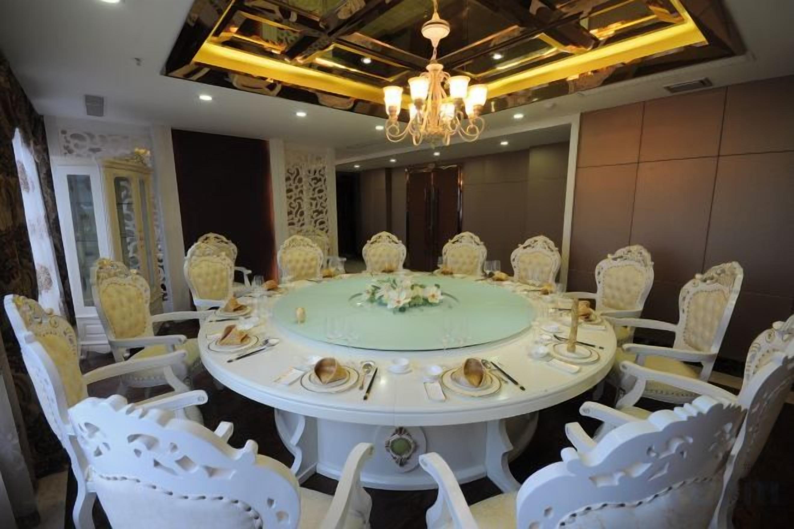 Mesa de jantar redonda com cadeiras brancas, um candelabro e um arranjo floral.