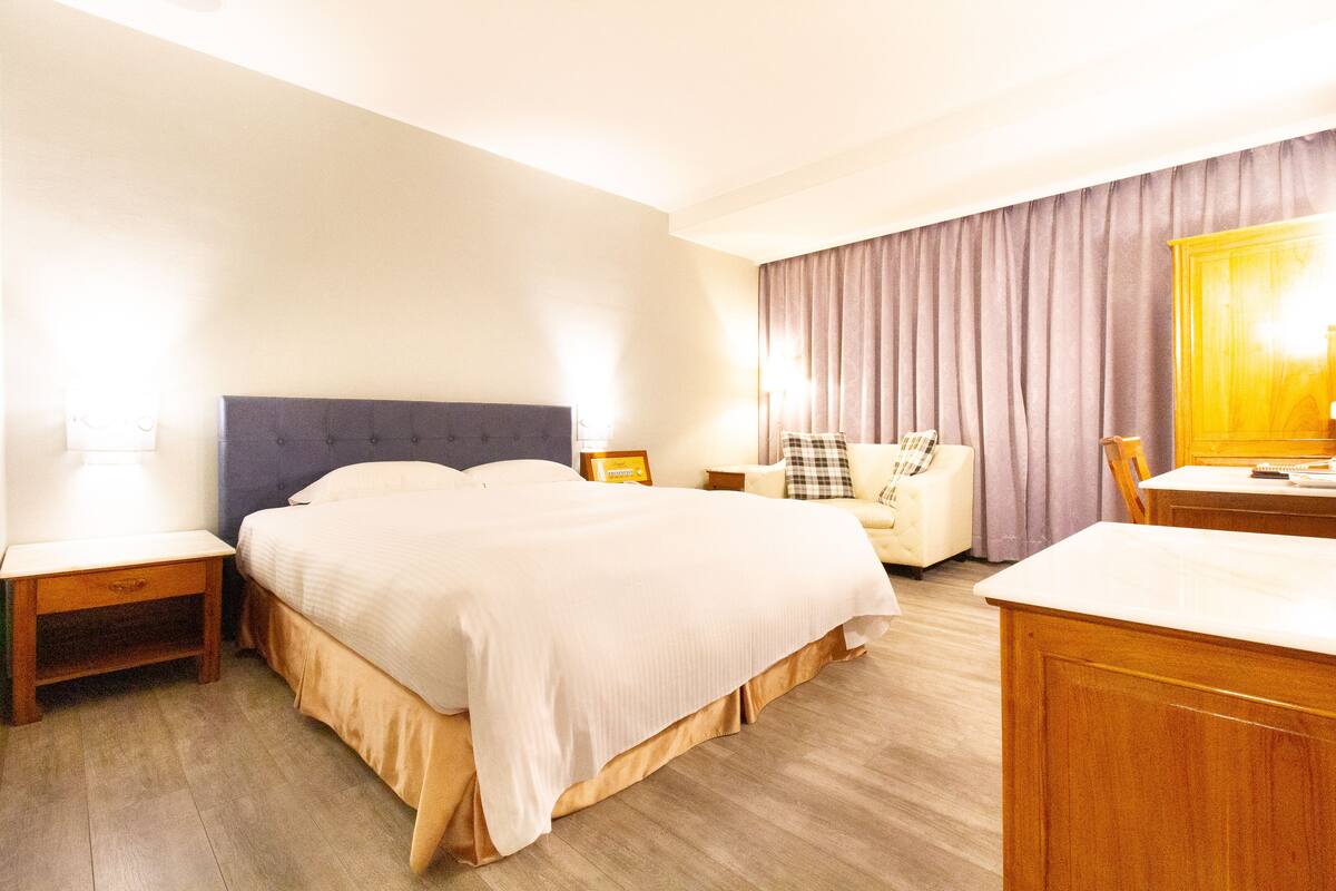 Quarto de hotel com uma cama grande, mesas de cabeceira, uma escrivaninha e uma cadeira.