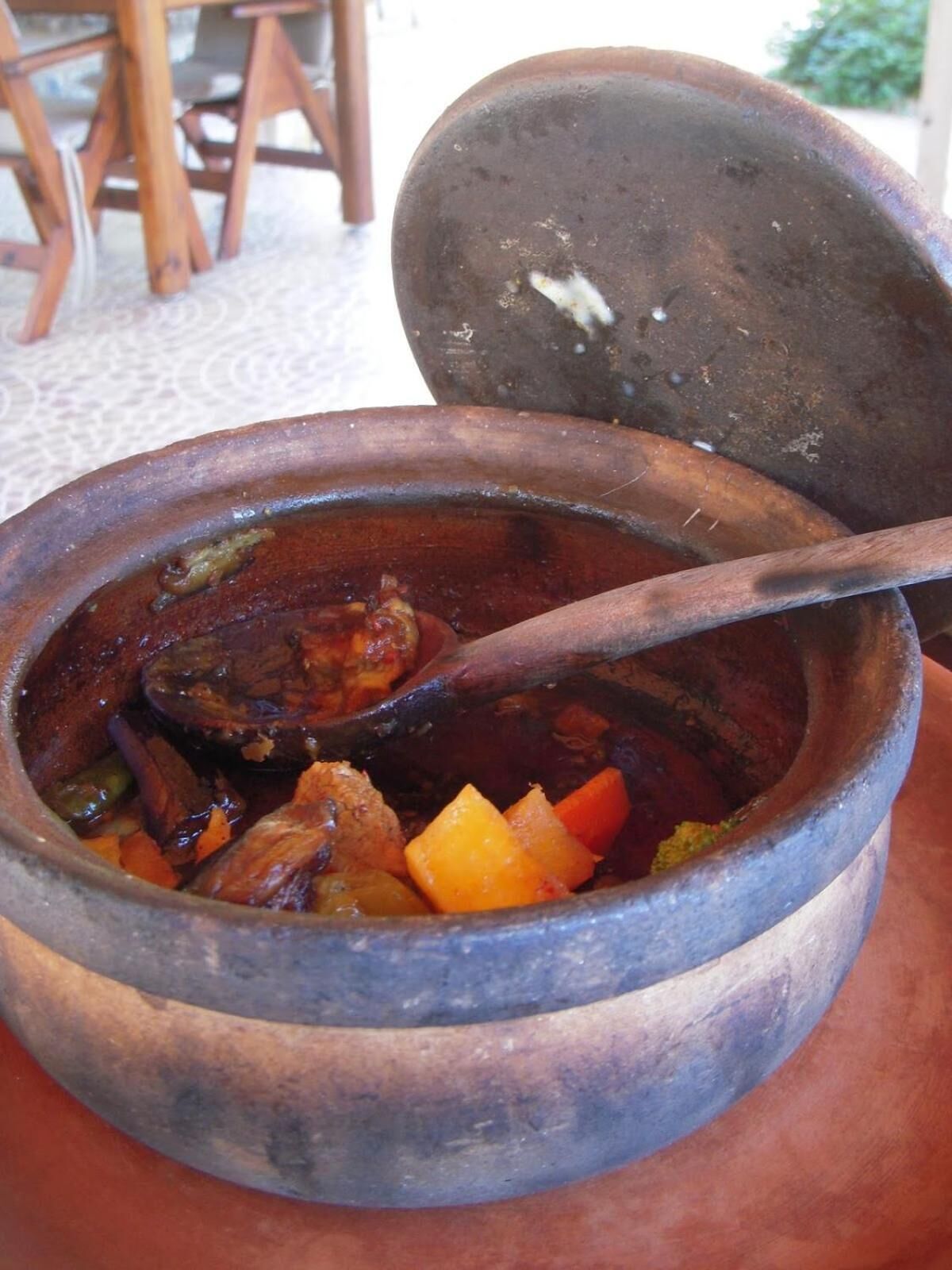 Um pote de barro rústico cheio de ensopado, com pedaços de carne e legumes.