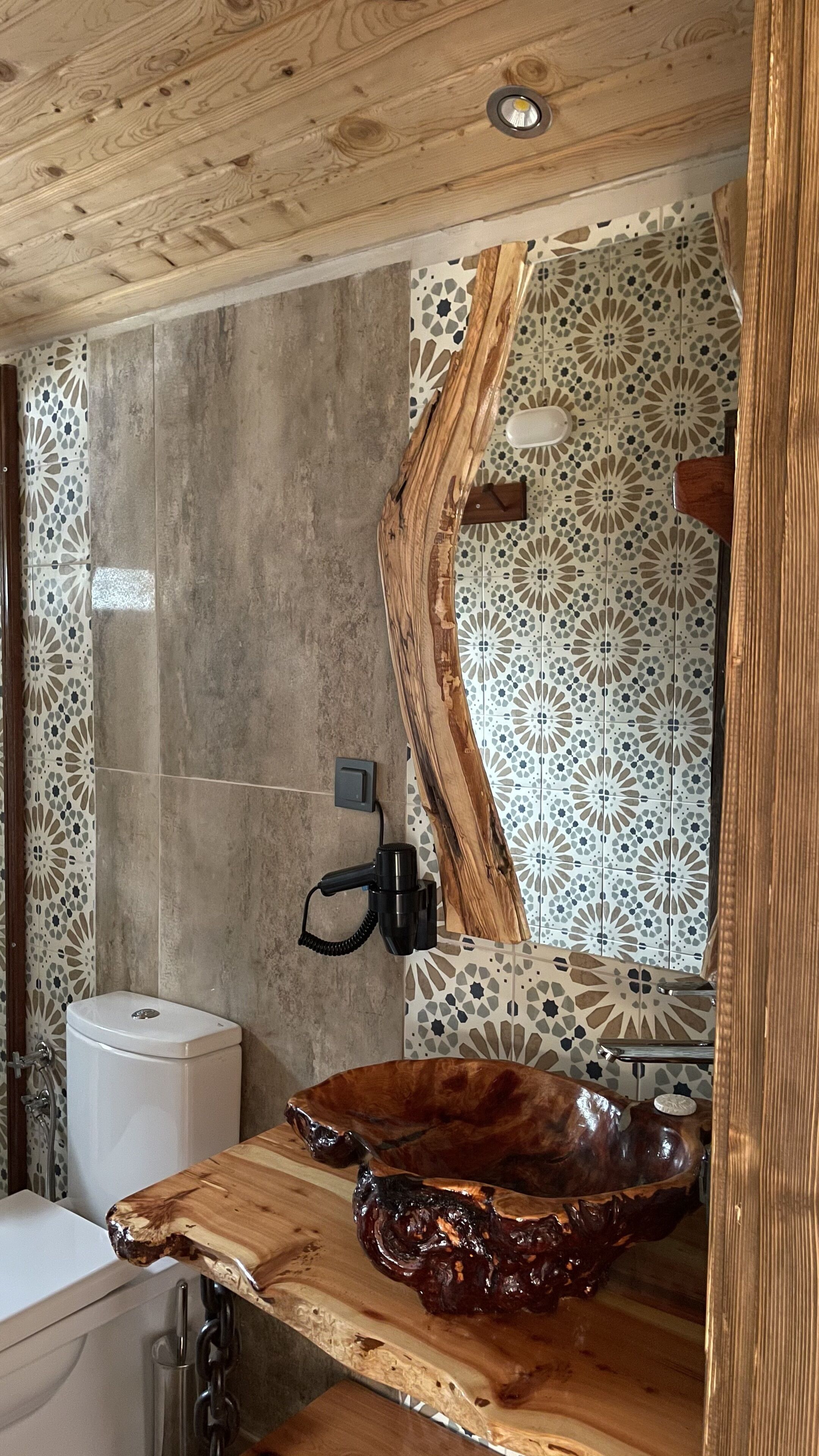 Casa de banho com toucador de madeira, sanita branca e espelho decorativo com moldura singular.