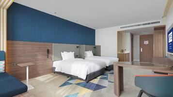 Quarto de hotel com uma cama grande, uma escrivaninha, uma cadeira e um banheiro visível por uma porta aberta.