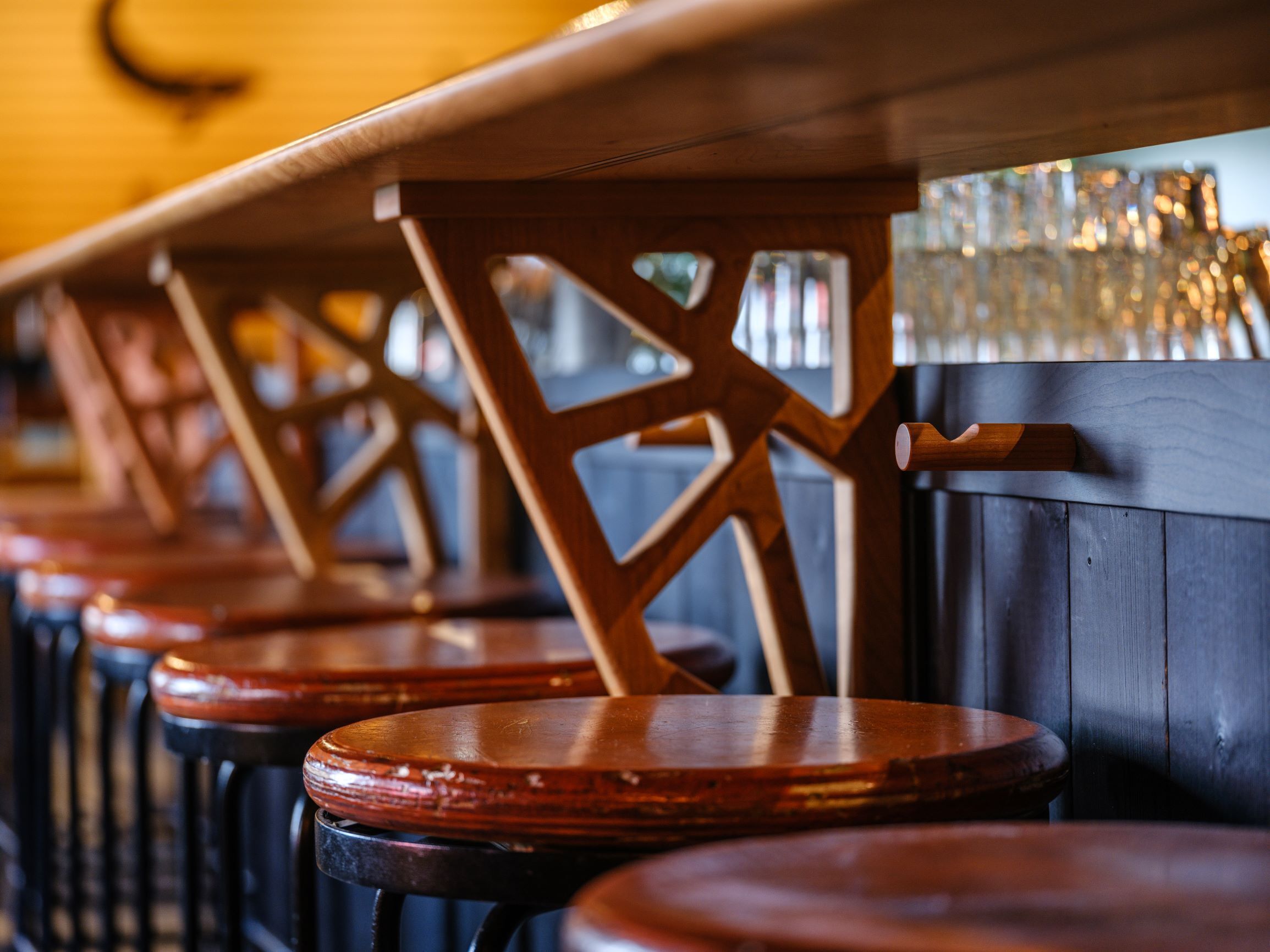 Fileira de banquetas de madeira com pernas de metal, dispostas num bar.