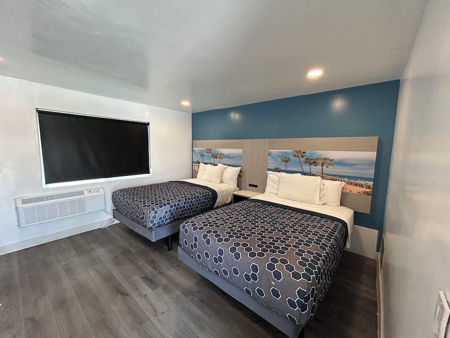 Quarto com duas camas, uma janela grande, ar-condicionado fixado na parede e um mural com tema de praia.