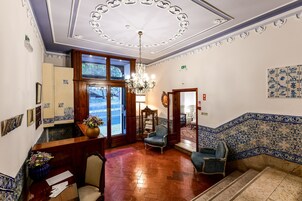 Um hall de entrada com um balcão de atendimento de madeira, duas poltronas, um candelabro e paredes com azulejos estampados.