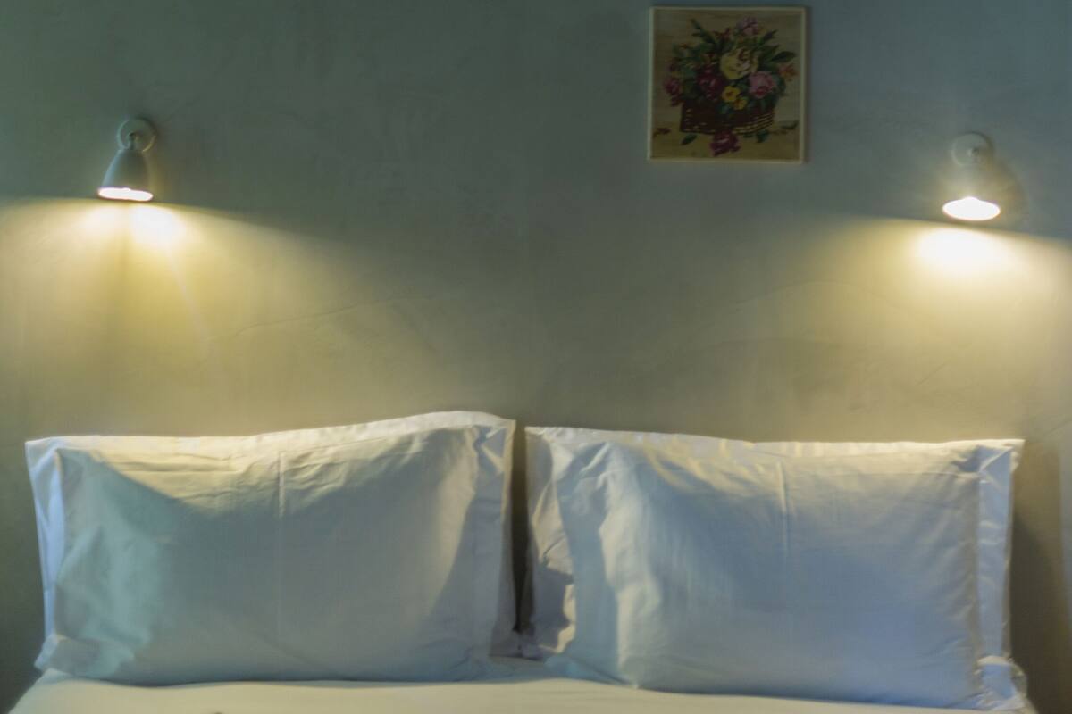 Quarto com uma cama, duas luminárias na parede e uma obra de arte floral.