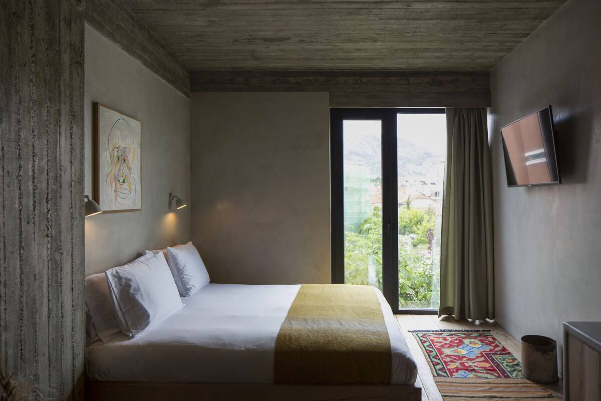 Quarto com cama, televisão e janela com cortinas.