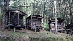 Três cabanas de madeira numa floresta, cada uma com uma escadaria que dá acesso à entrada.