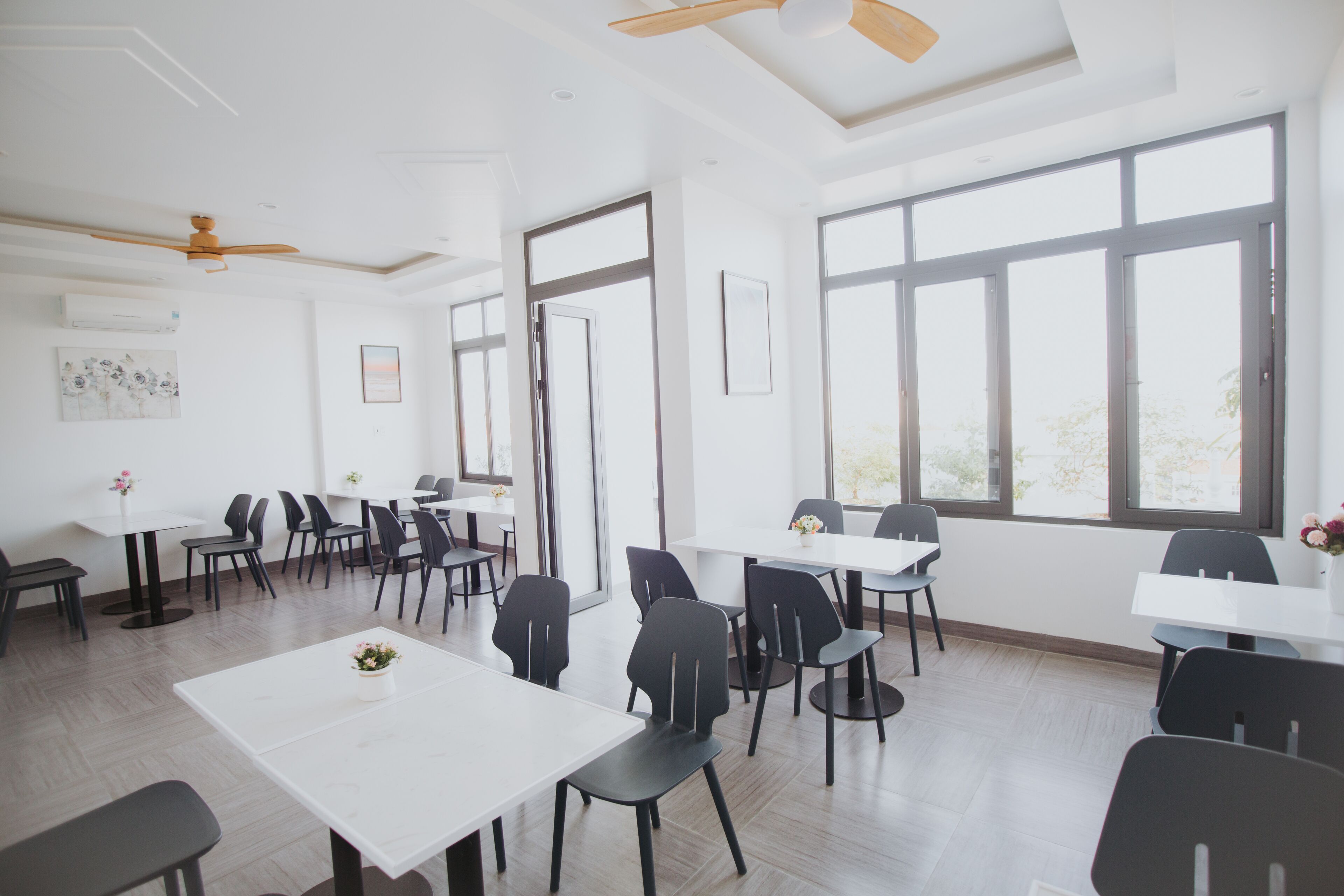 Uma sala de conferências moderna com mesas brancas e cadeiras pretas, grandes janelas e ventiladores de teto.