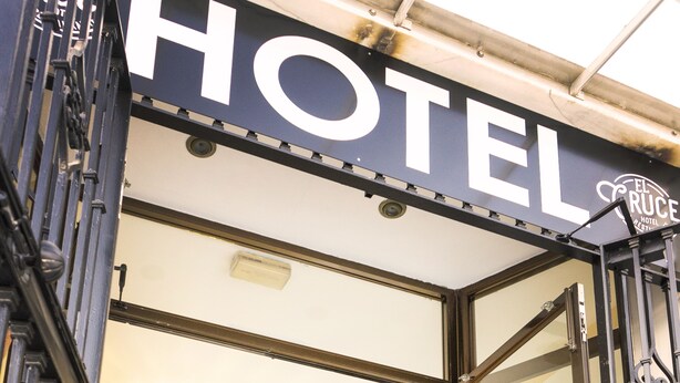Entrada de hotel com uma grande placa com a palavra "HOTEL" e uma receção visível no interior.