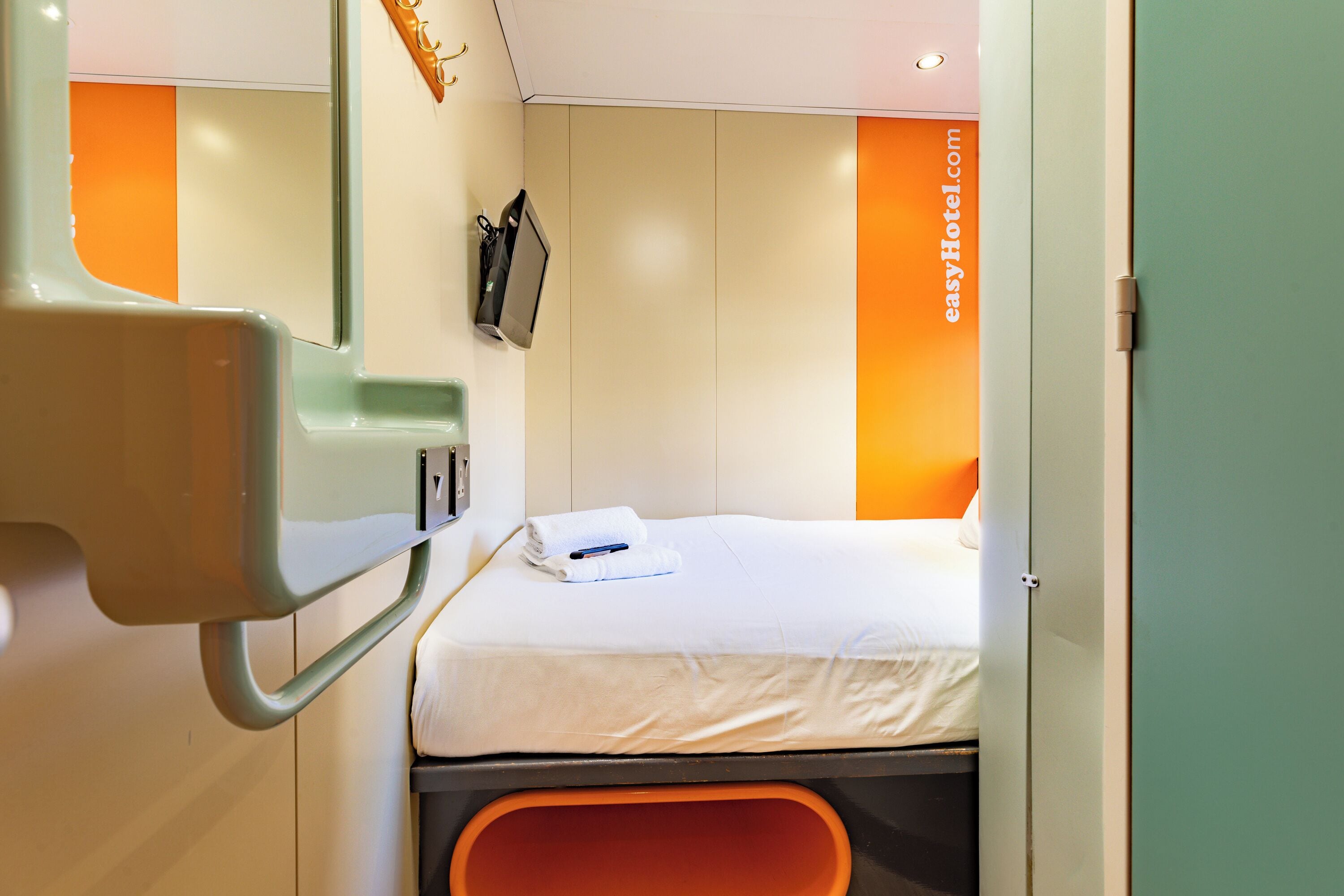Quarto de hotel com cama, mesa de cabeceira, televisão na parede e toalha sobre a cama.