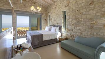 Quarto com parede de pedra, uma cama, um sofá, um candelabro e vista para a paisagem.
