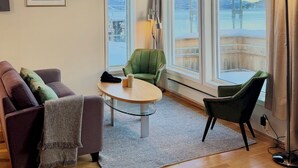 Uma sala de estar moderna com sofá, poltronas, mesa de centro e grandes janelas com vista para uma ponte e para a água.