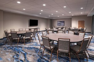 Sala de conferências com uma grande mesa oval rodeada por cadeiras, uma televisão de tela plana na parede e piso coberto de carpete.